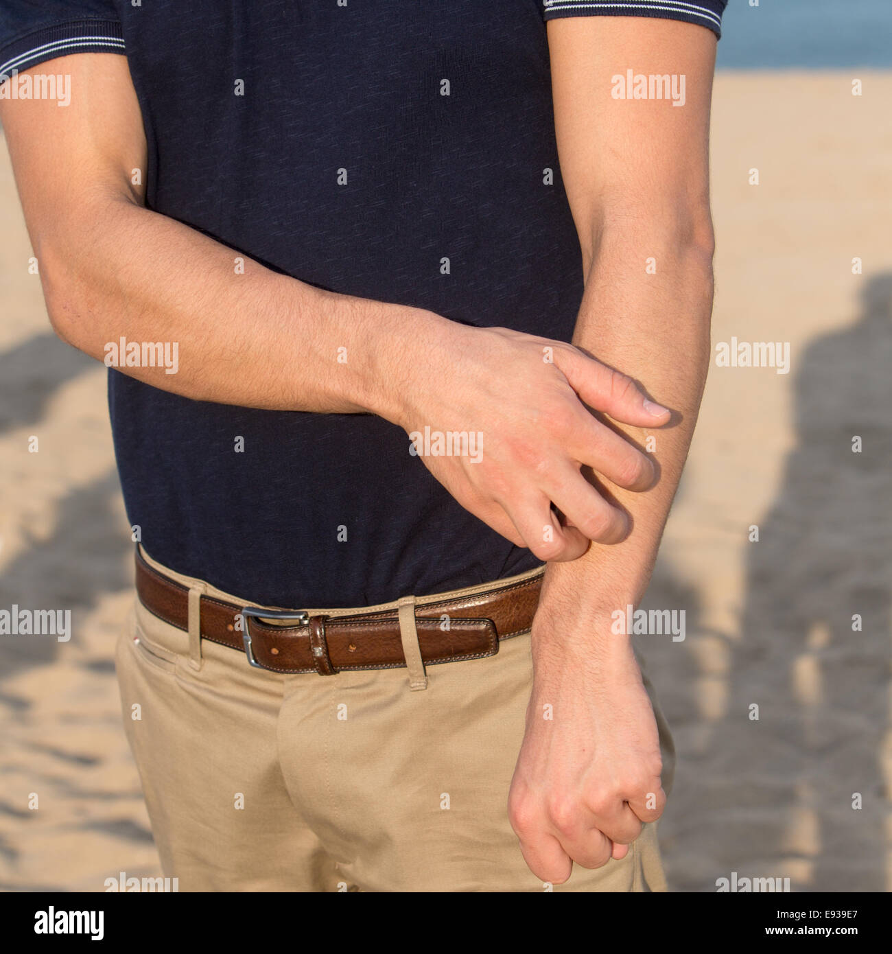 Man rubs arm on the beach Stock Photo - Alamy