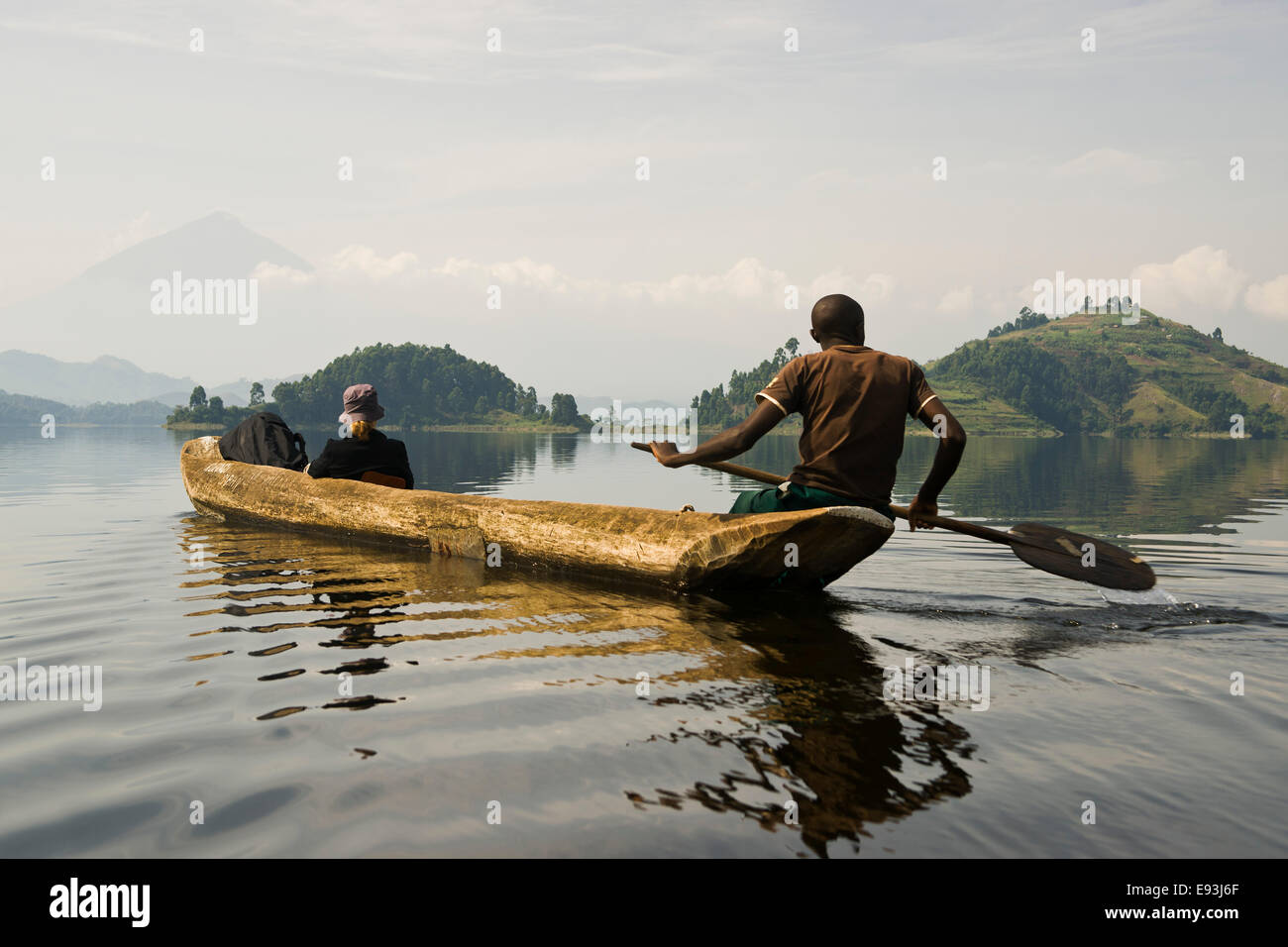 Guide and woman in canoe in the morning mist by Mutanda Lake in front ...