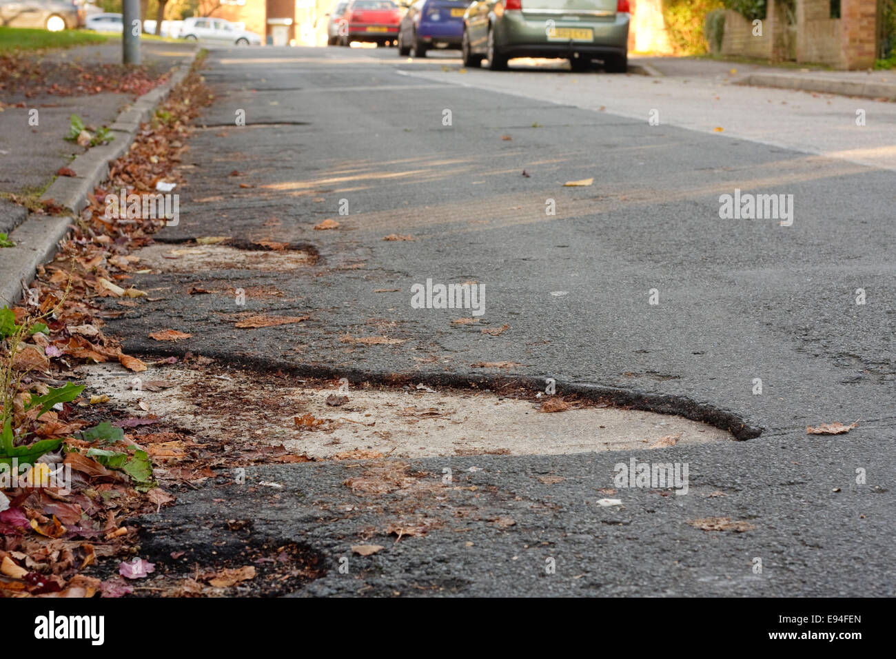 A large pot hole on a road with parked cars in the background Stock ...