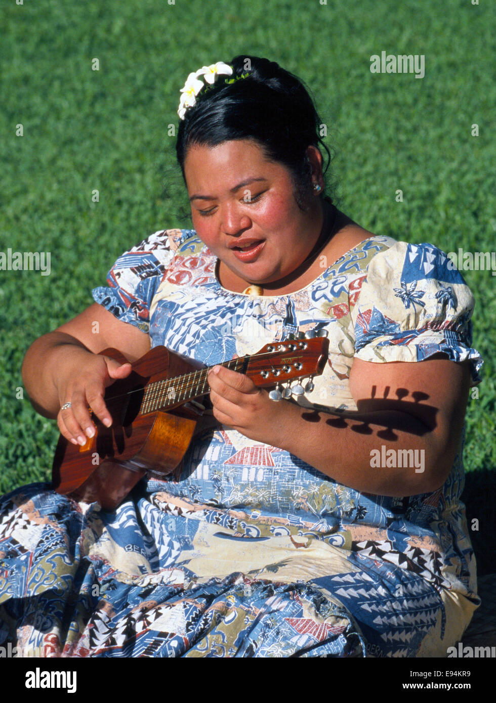 A young Hawaiian woman in Honolulu, Hawaii, USA, sings and strums an ...