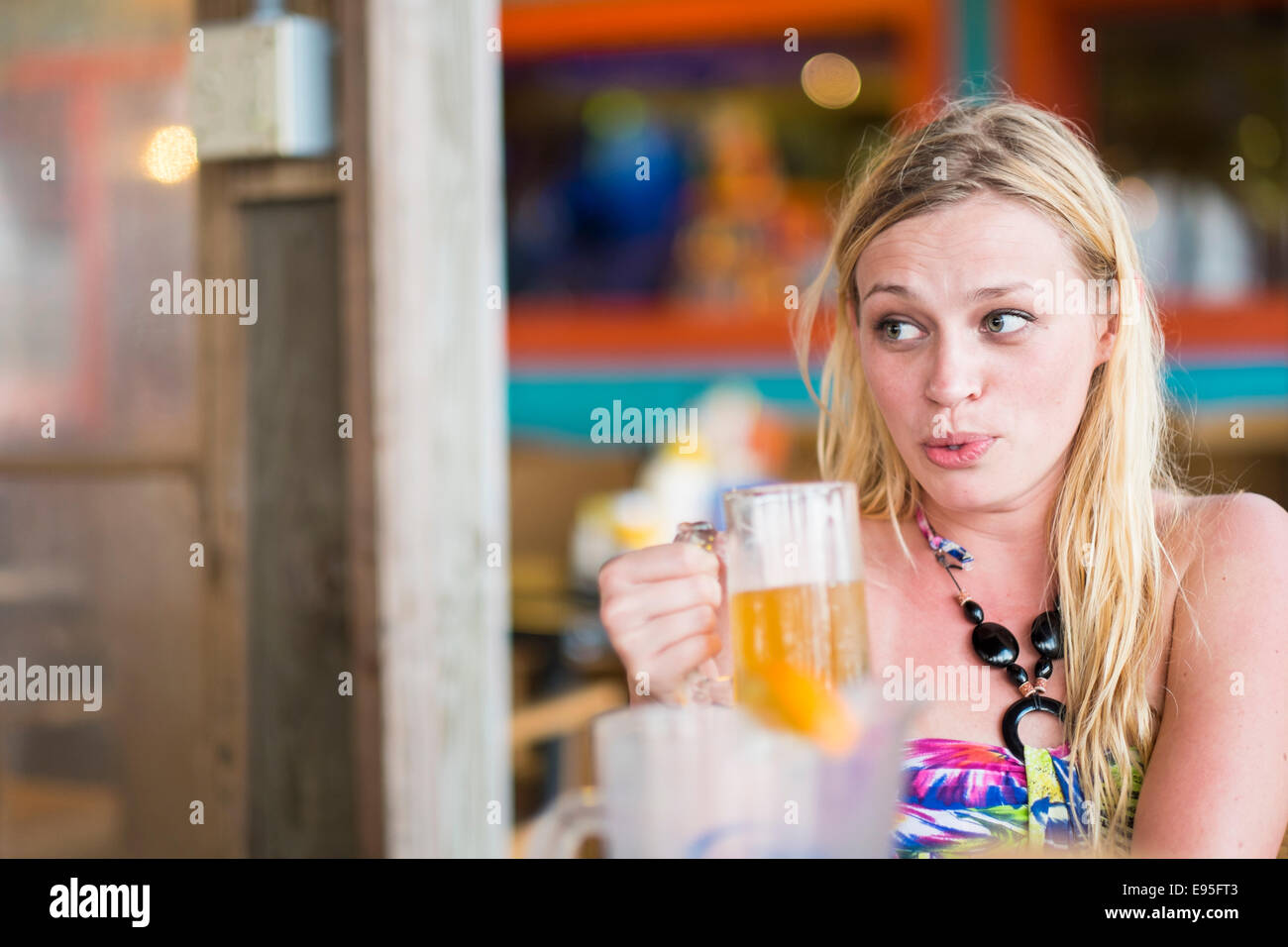 Young woman drinking beer in outdoor bar looking away making funny face ...