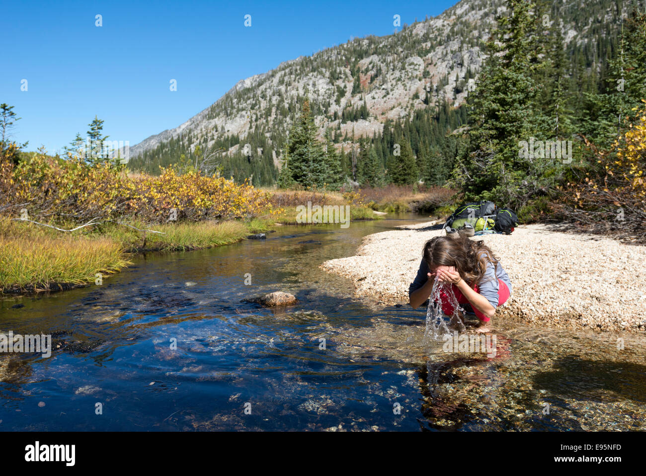 Woman splashing water on her face from a stream in Oregon's Wallowa ...