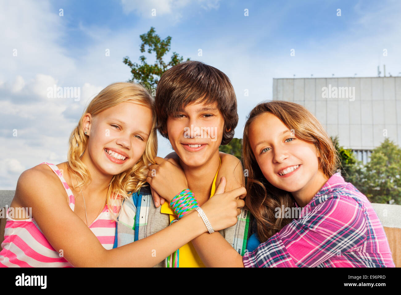 Two girls embracing boy's neck and smile happily Stock Photo - Alamy