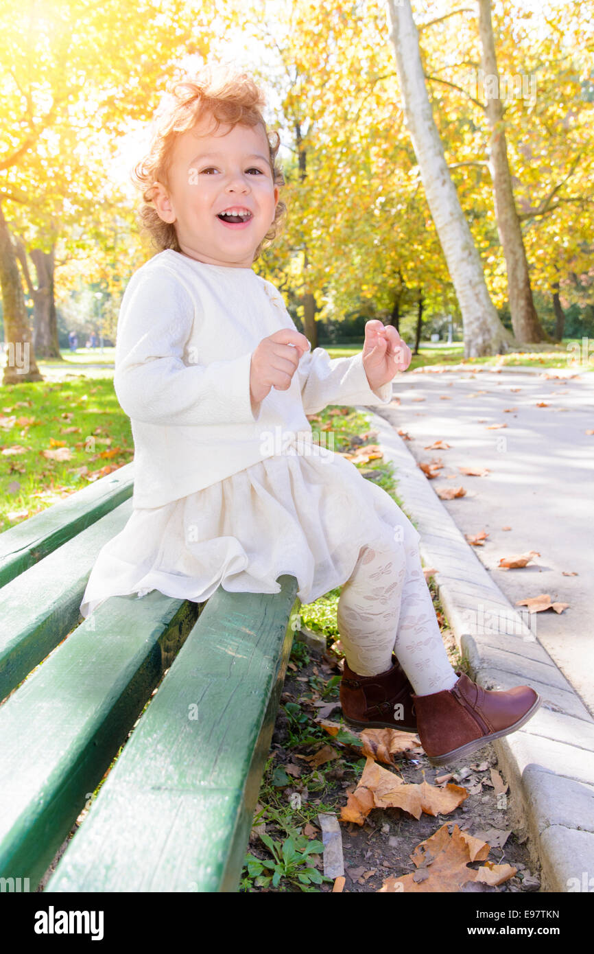 Happy little girl sitting on bench in the park Stock Photo - Alamy