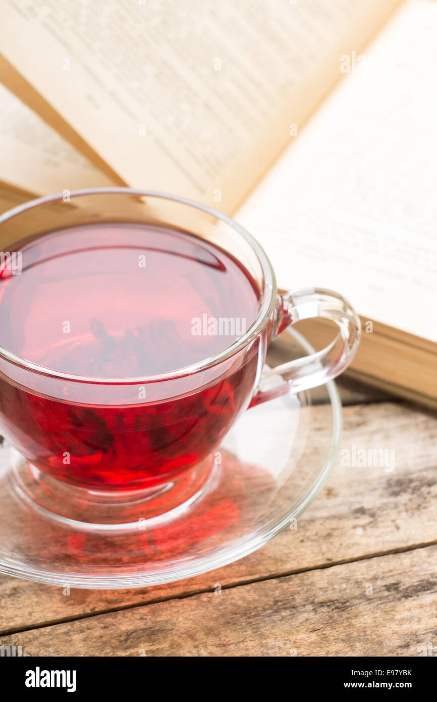 Glass cup of Karkade tea with old opened book at the wooden table ...