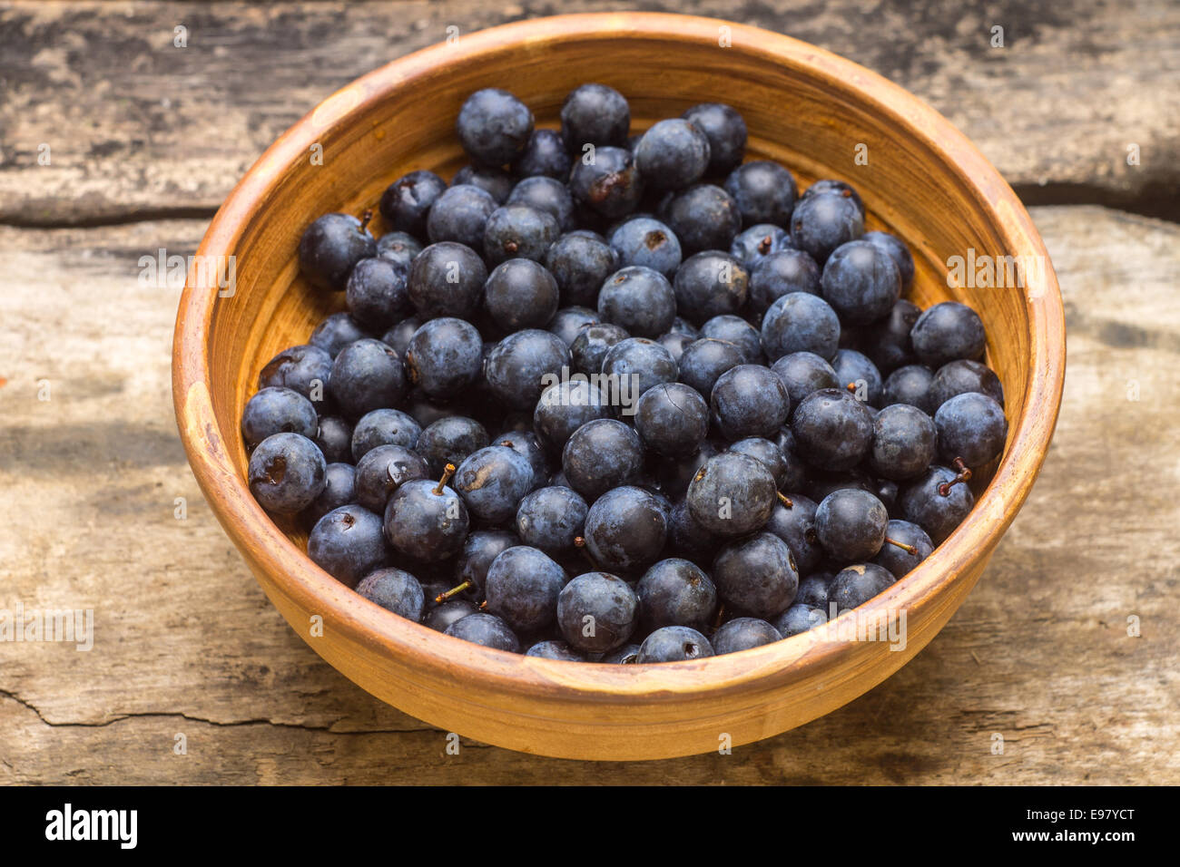 Fresh wild berries in clay bowl on wooden background. Blackthorn berry ...