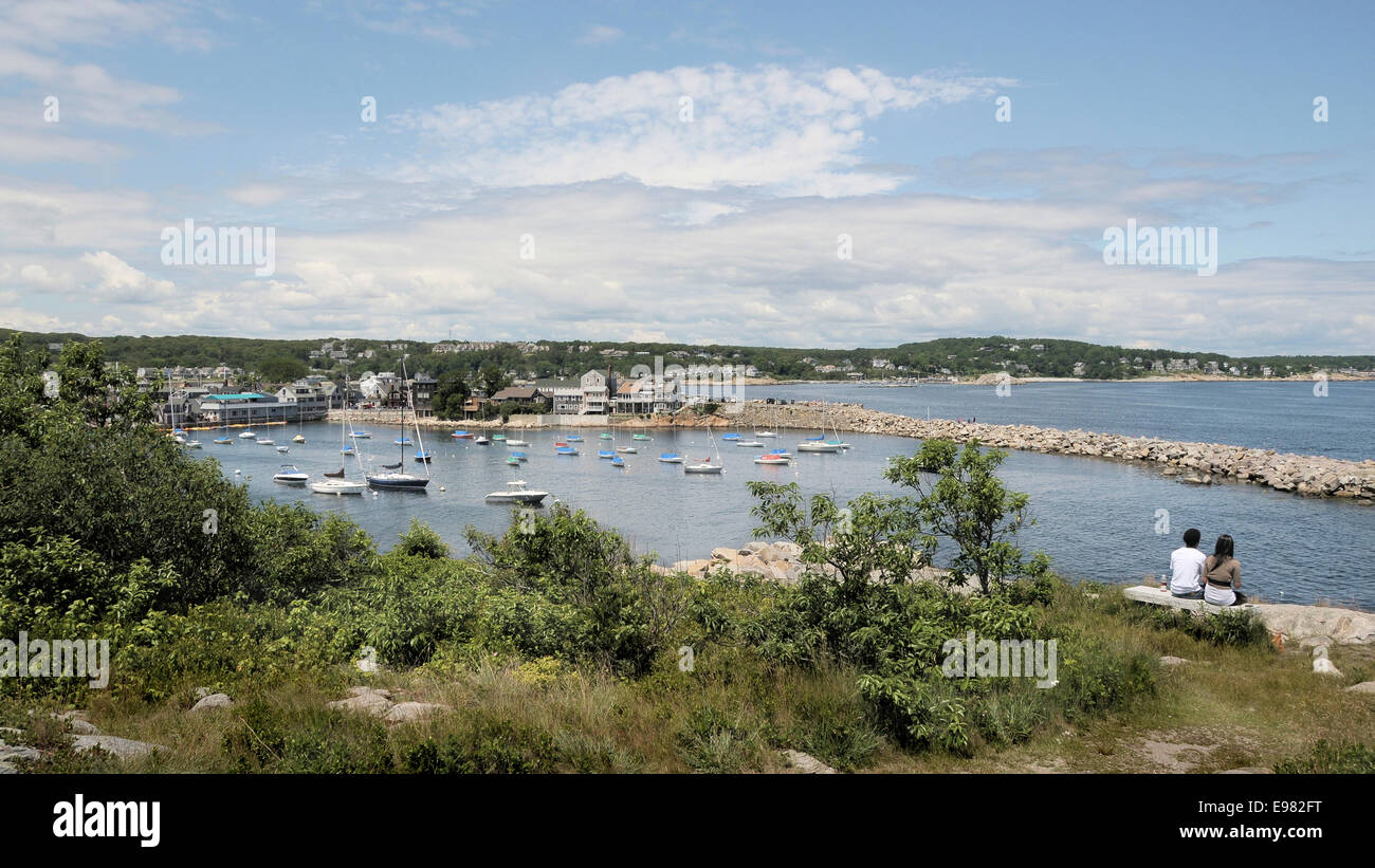 A young couple sitting on hillside are looking downward at Rockport Bay ...