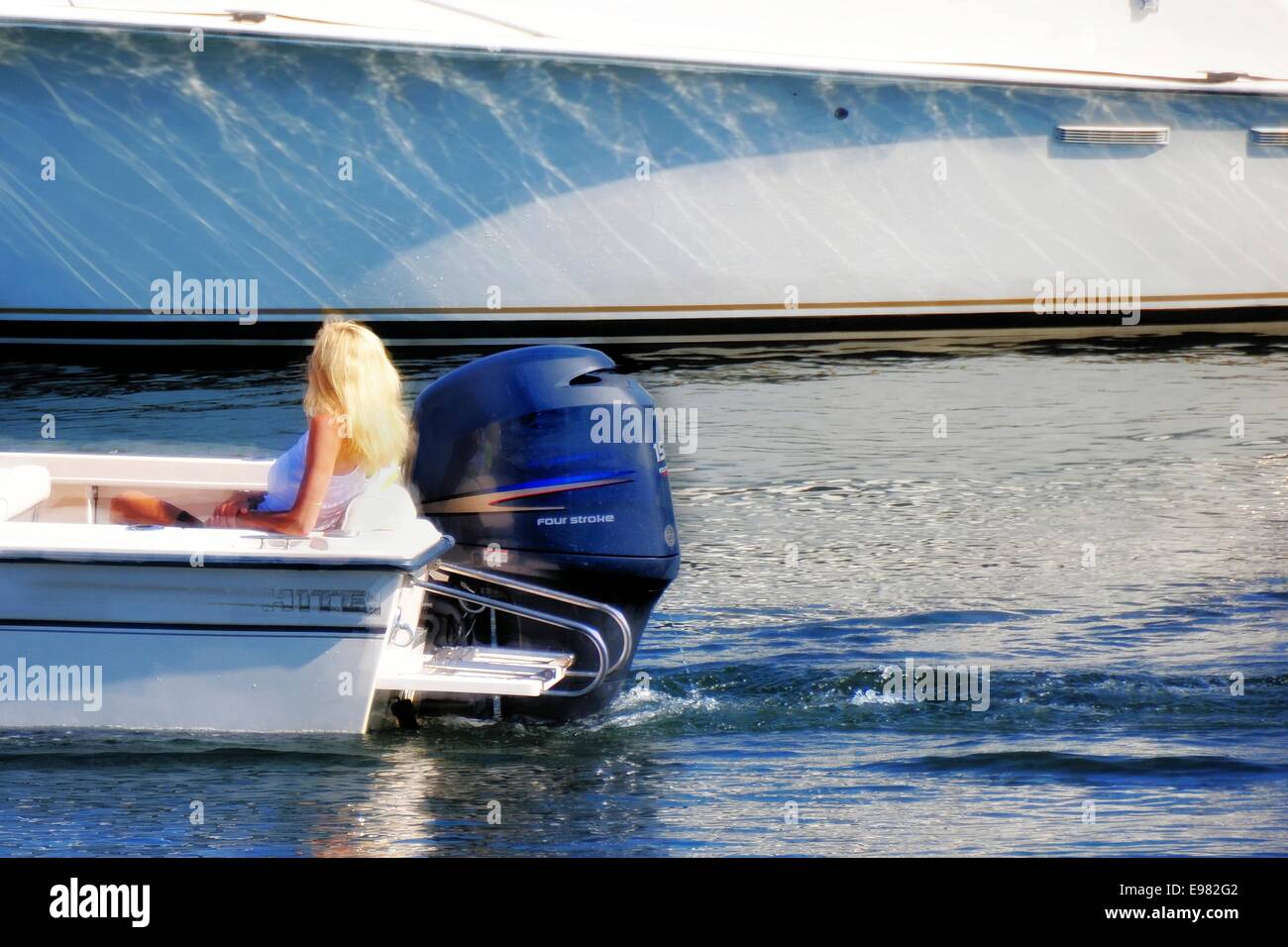 Blonde women sitting in back powerboat next to large blue outboard ...