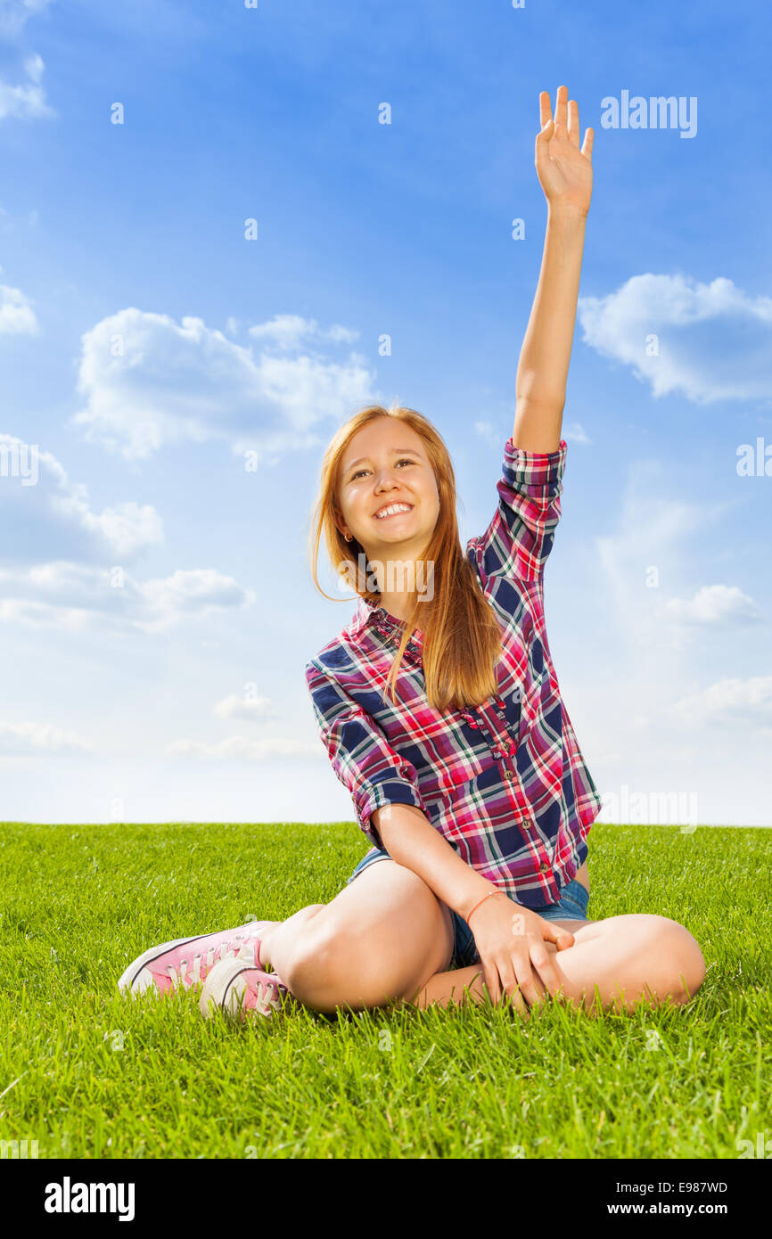 Girl with hand up in air sitting on green grass Stock Photo - Alamy