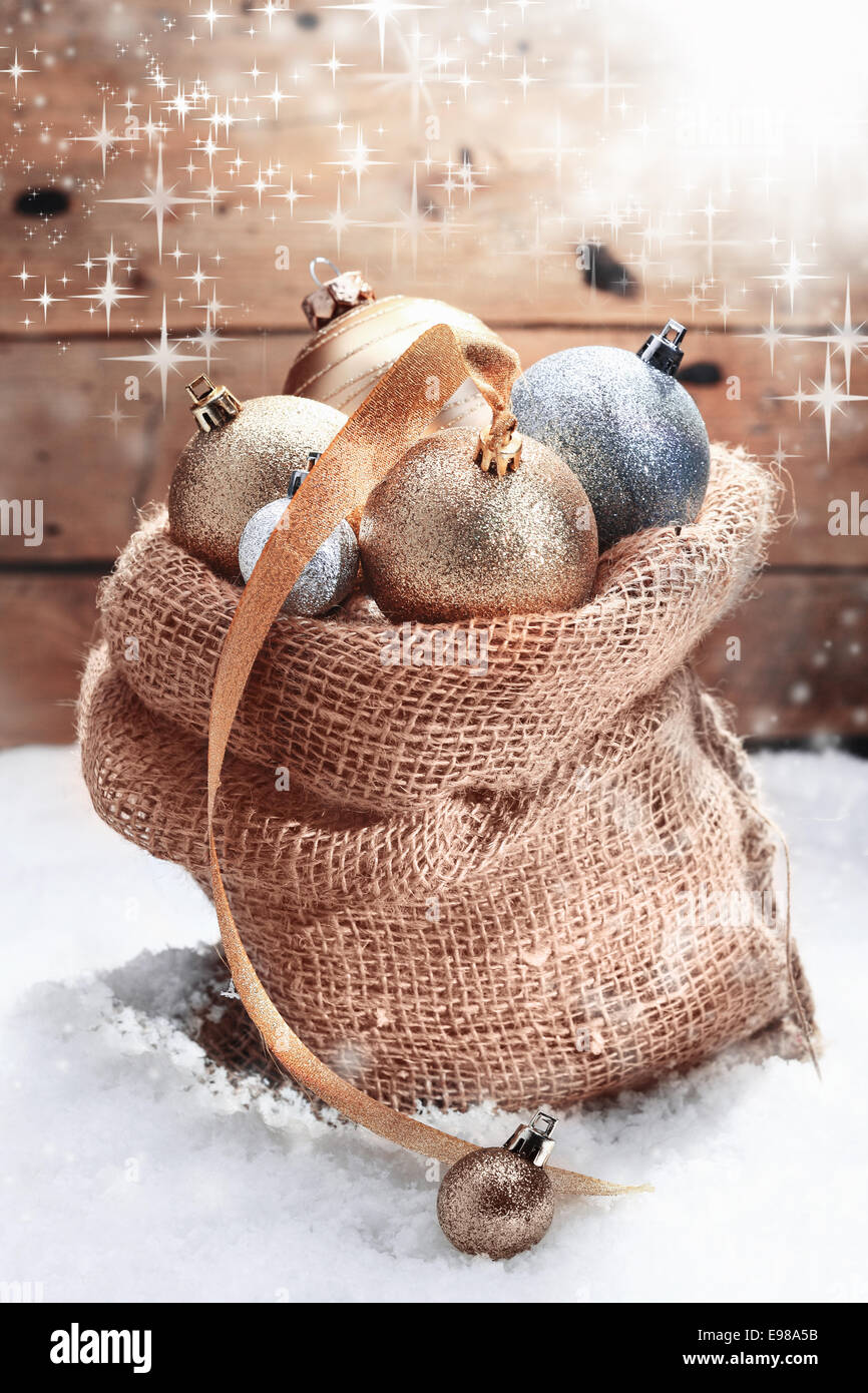 Decorative Christmas baubles piled high in a hessian bag on winter snow ...