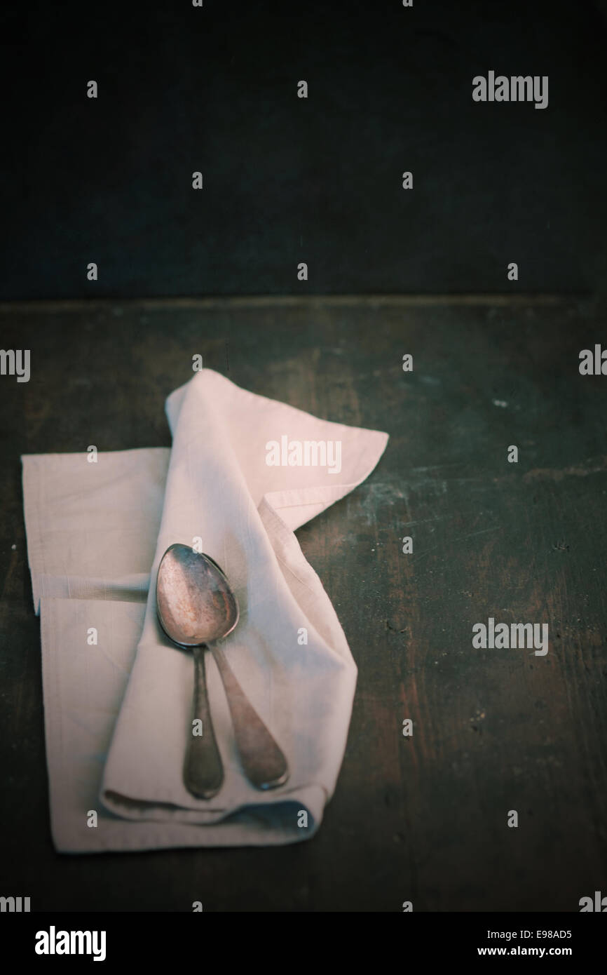 Folded plain white linen napkin and teaspoons on an old dark wooden ...