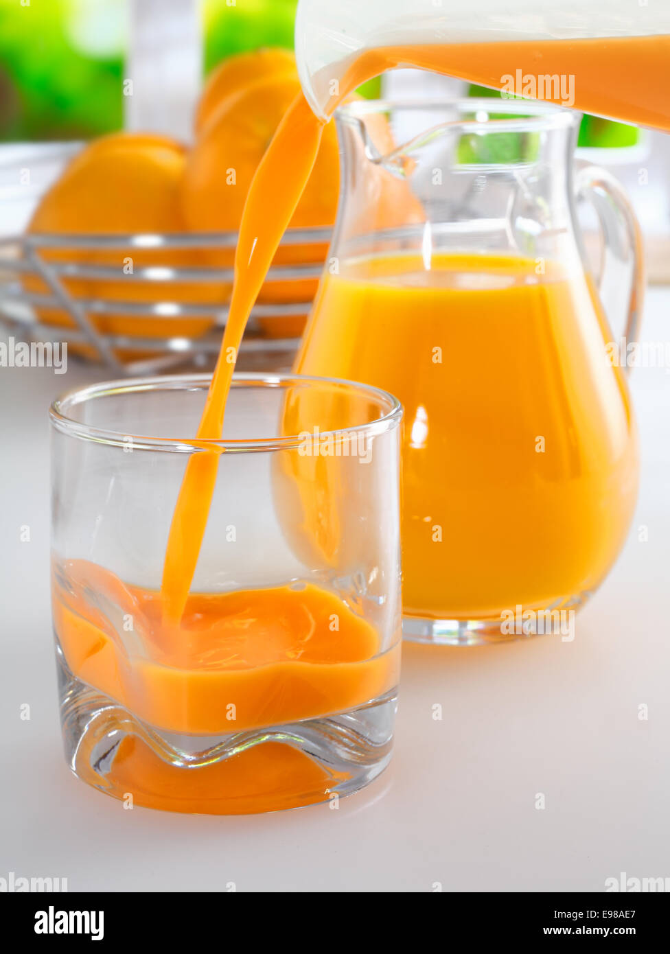 Pouring a glass of fresh healthy orang juice from a jug with a full ...