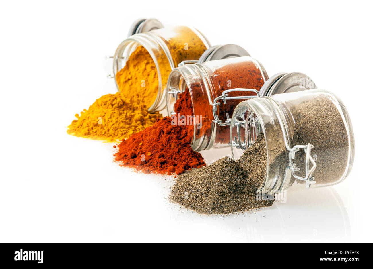 Colourful ground spices spilling from glass jars onto a white ...