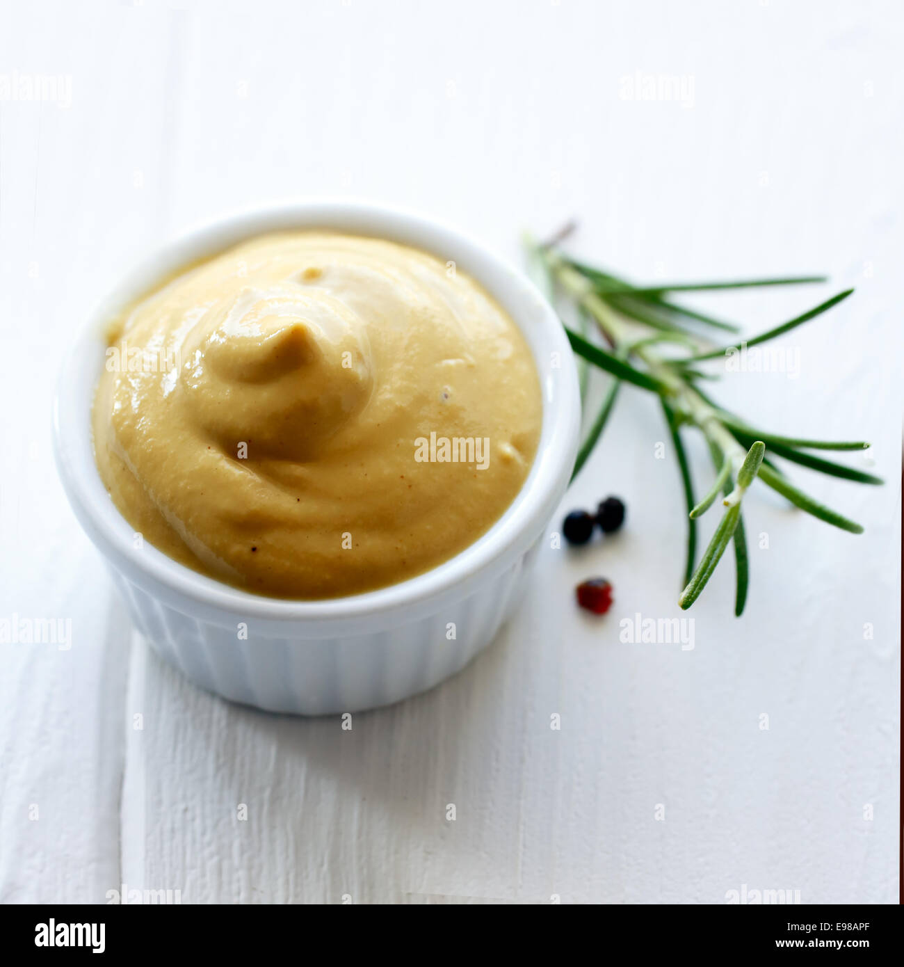 Small ramekin of mustard with a sprig of rosemary against white Stock ...