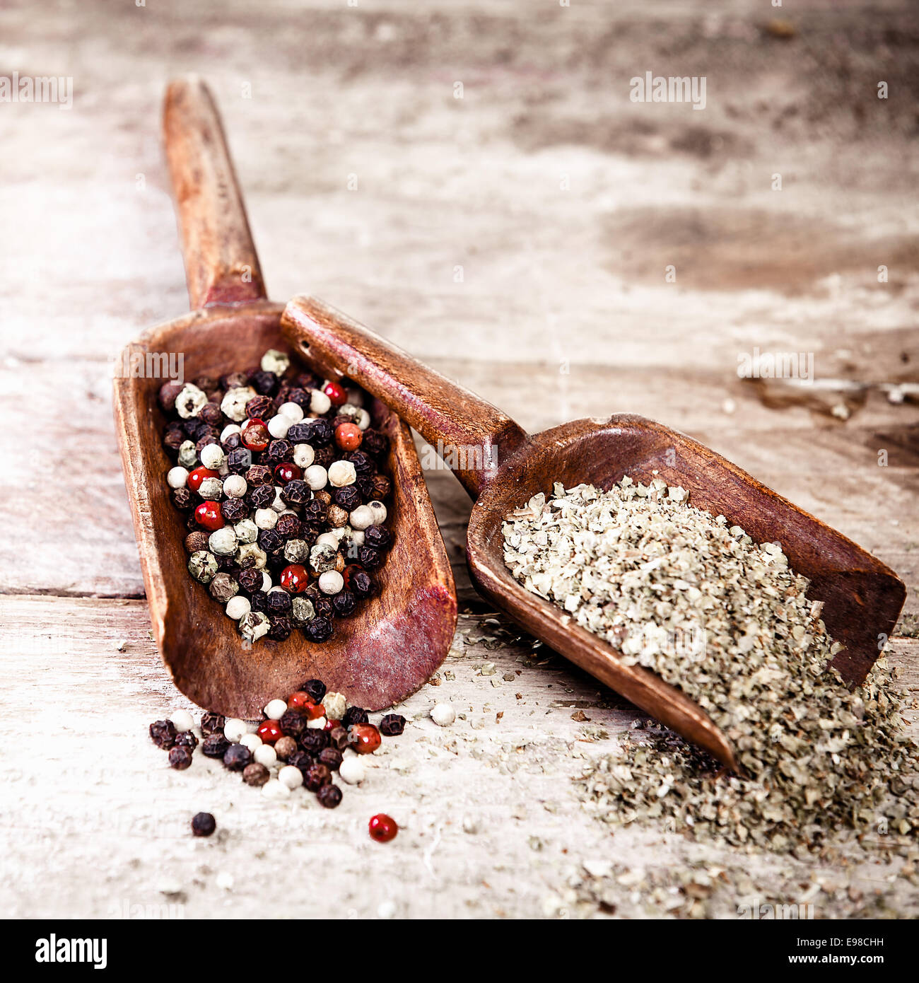 Mixed whole dried peppercorns spilling out of a small wooden scoop for ...