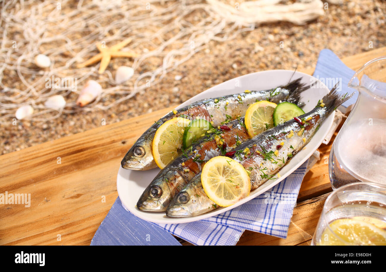 Three grilled sardines on a platter over a table outdoors on the beach ...