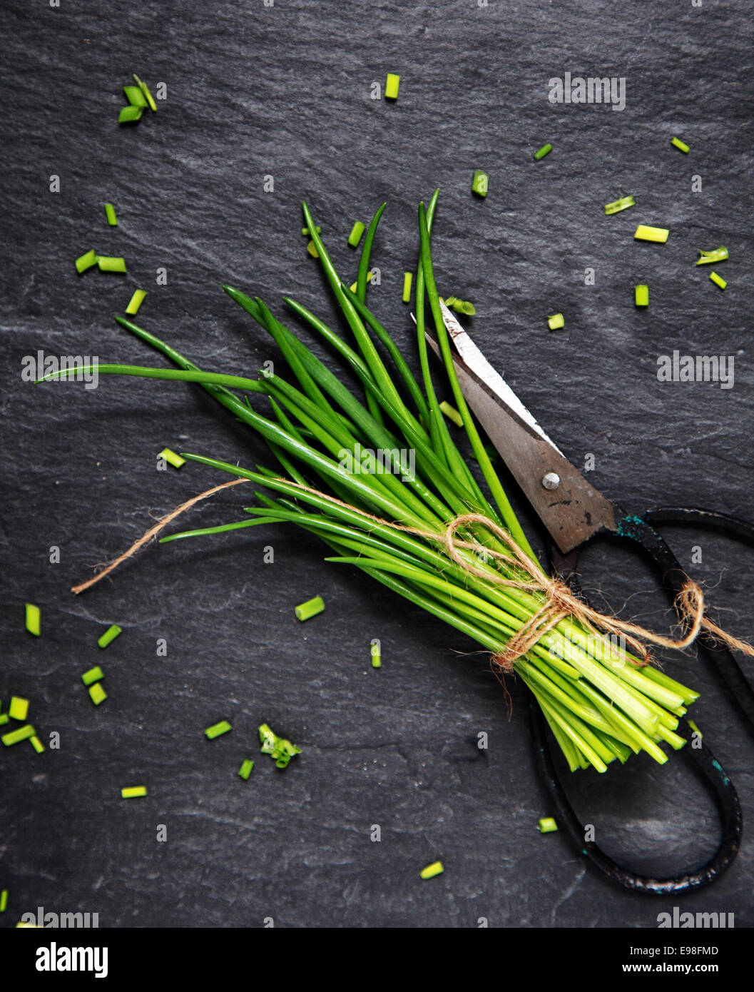 Chopping a bunch of fresh chives with scissors on a slate kitchen ...