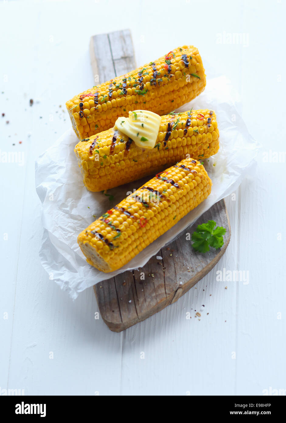 Grilled corn on the cob topped with a butter curl and served at a ...