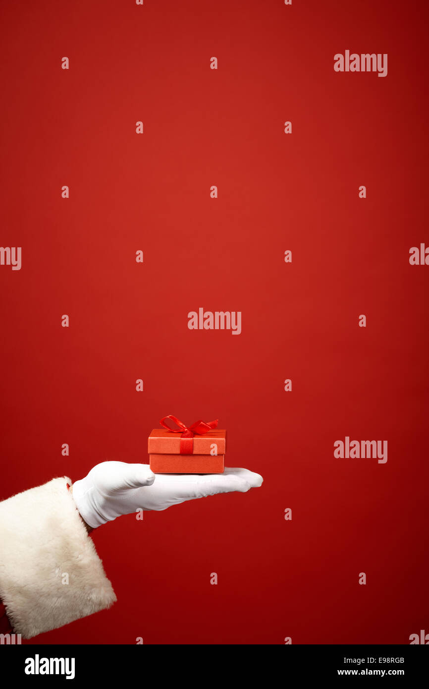 Santa Claus gloved hand with small package over red background Stock ...