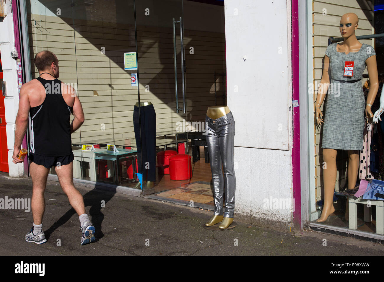 Weird street scene with silver trousers outside a shop as people pass ...