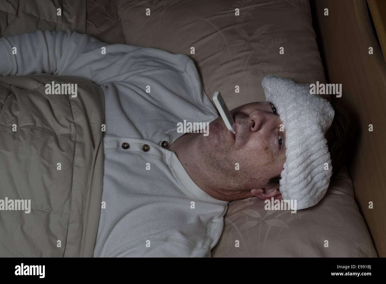 Horizontal image of mature man, with wet towel on forehead, lying down ...