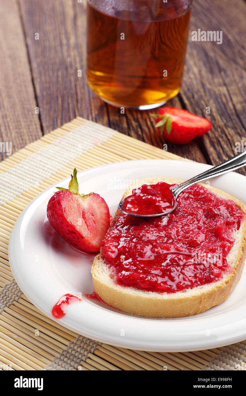 Bread with red strawberry jam and cup of tea on wooden table Stock ...