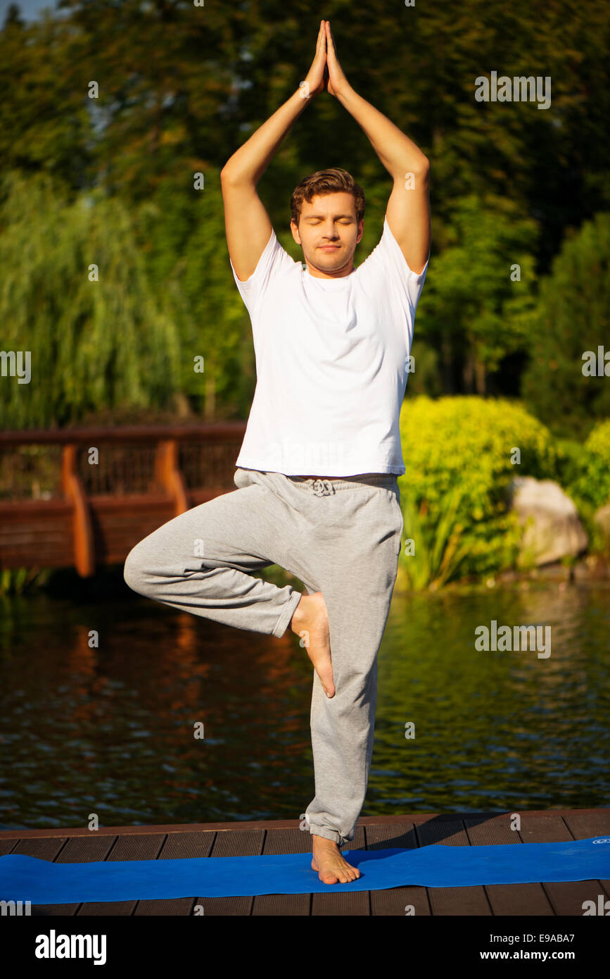 Young man practicing yoga, doing tree pose Stock Photo - Alamy
