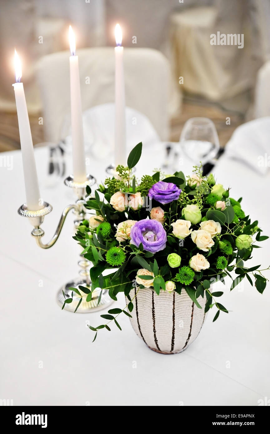 Floral arrangement and a candlestick with lit candles on a dinner table ...