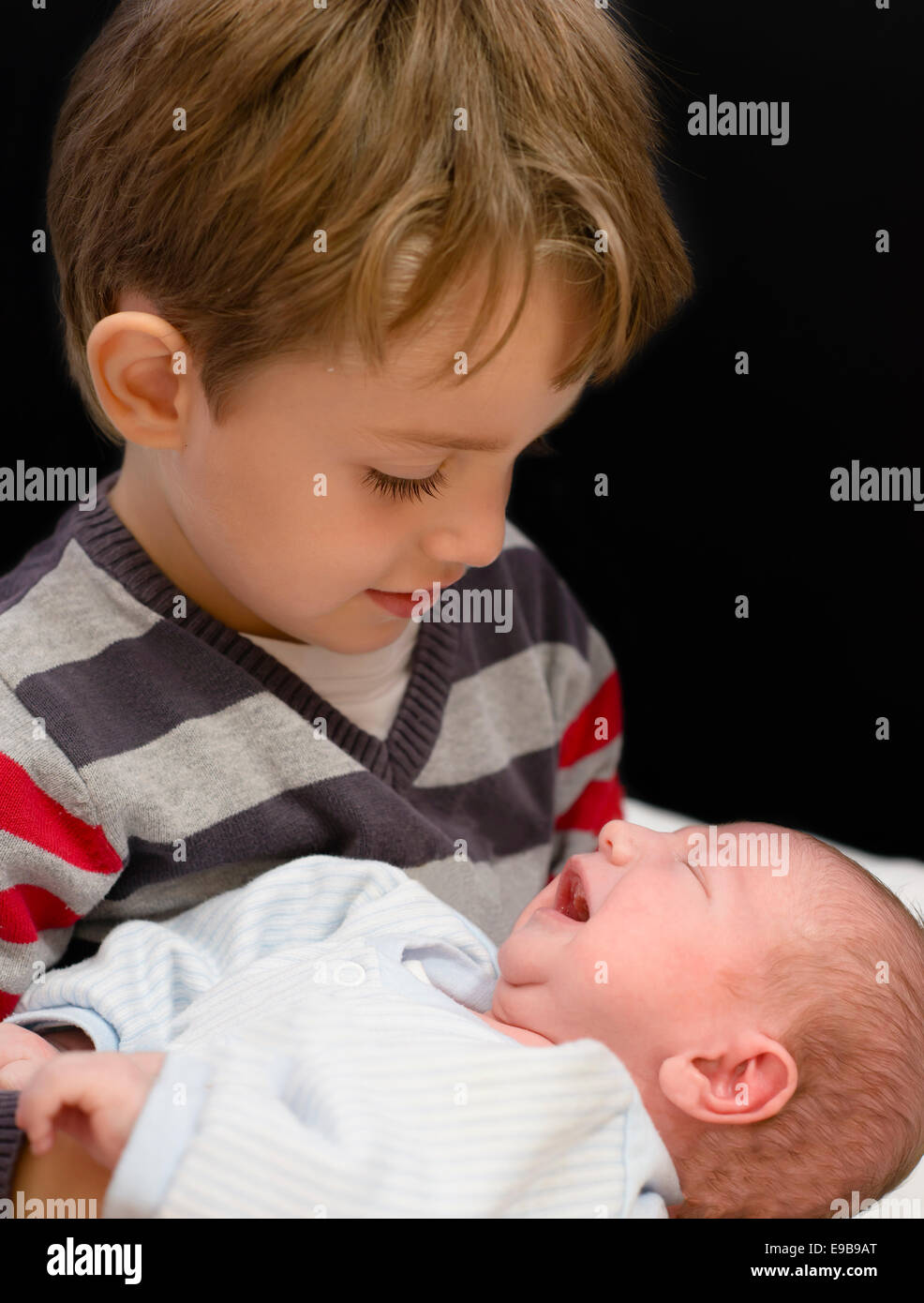 Curious Boy holding his little brother, black background Stock Photo ...