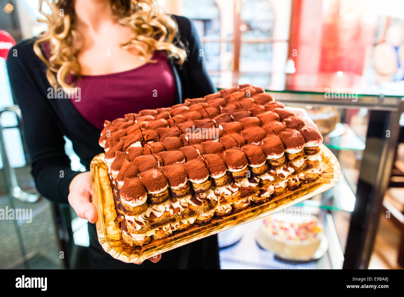 Female confectioner presenting tray of cake in bakery or pastry shop ...