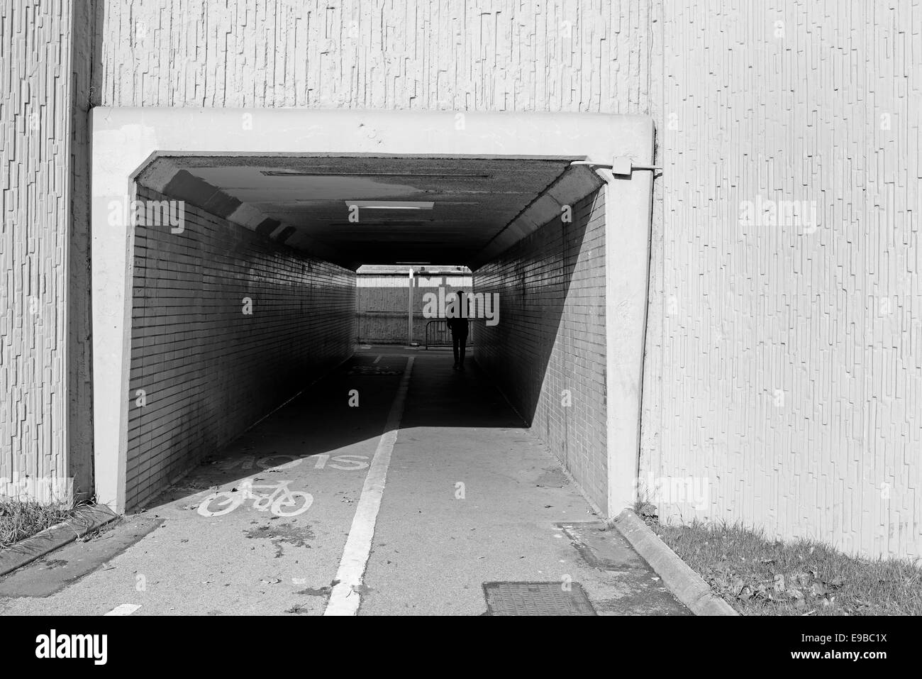A young woman silhouetted walking through a city underpass on a sunny ...