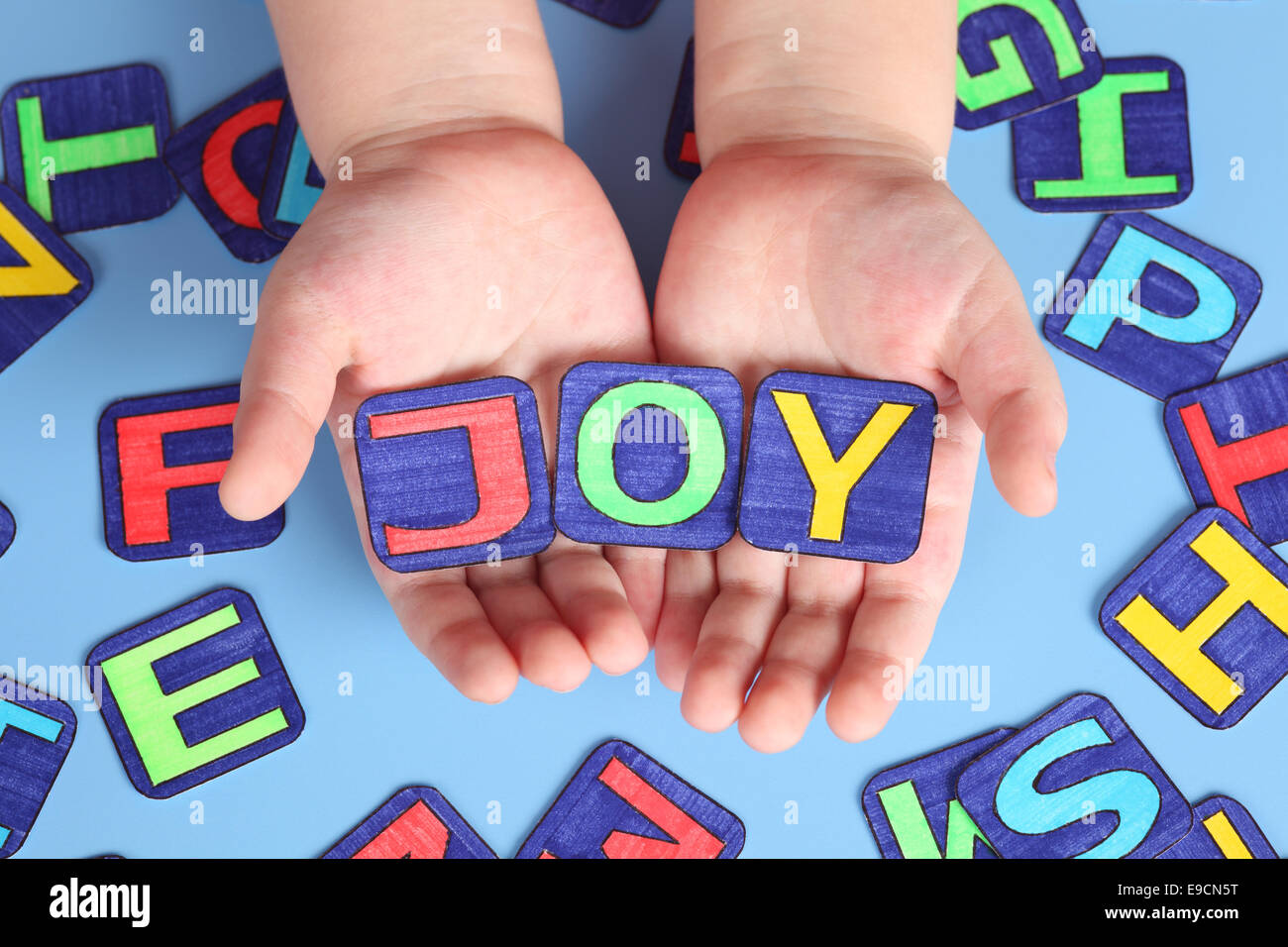 Word "Joy" in child's hands with letters on blue background. Letters ...