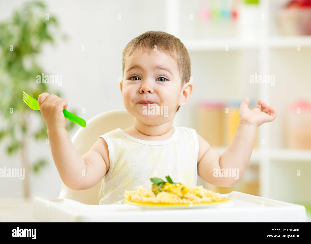 one year old kid boy in a highchair for feeding with a fork and Stock ...