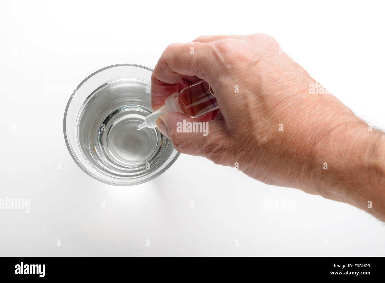 Man's hand putting drops of pharmacy in a glass of transparent water ...
