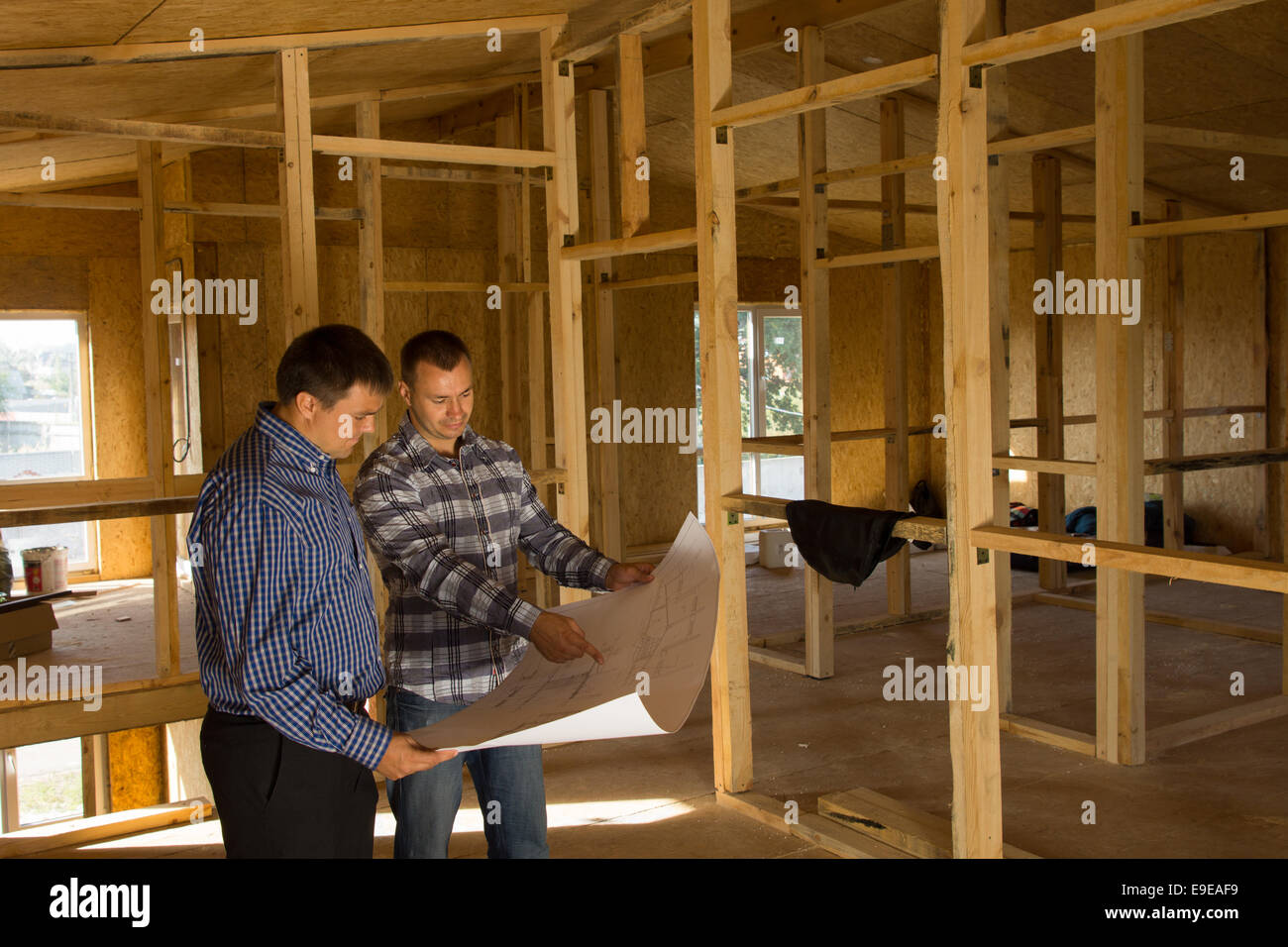 Two builders standing with an open blueprint discussing the interior of ...