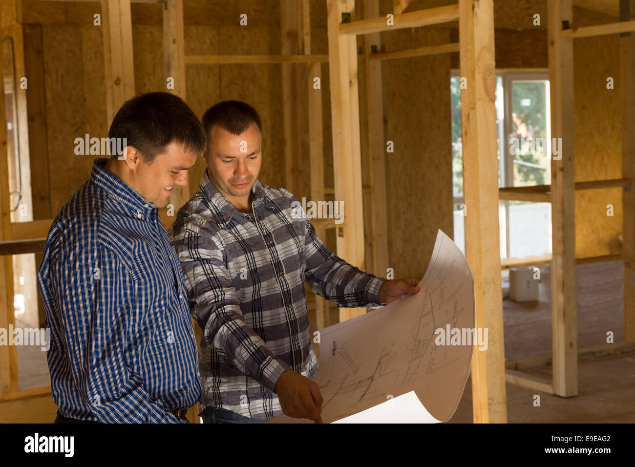 Two builders inside a half completed timber frame house standing having ...