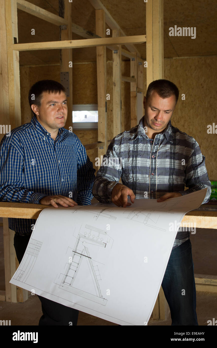 Two builders checking a blueprint together as they standing inside a ...