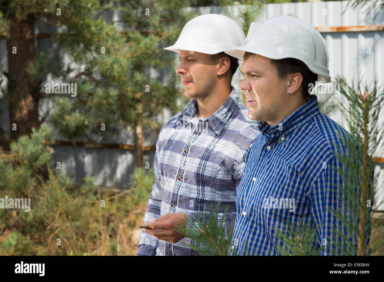 Two engineers with serious expressions standing together on a building ...