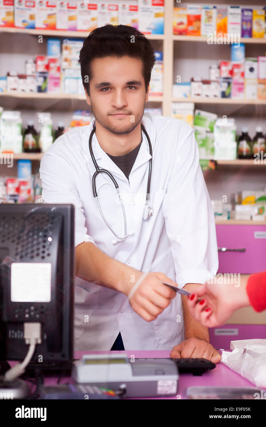 Smiling doctor giving credit card to customer in a pharmacy. Customer ...