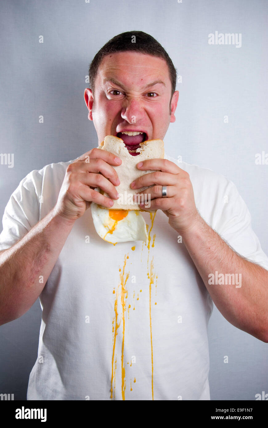 a man eats a fried egg sandwich while half of it spills out of the ...