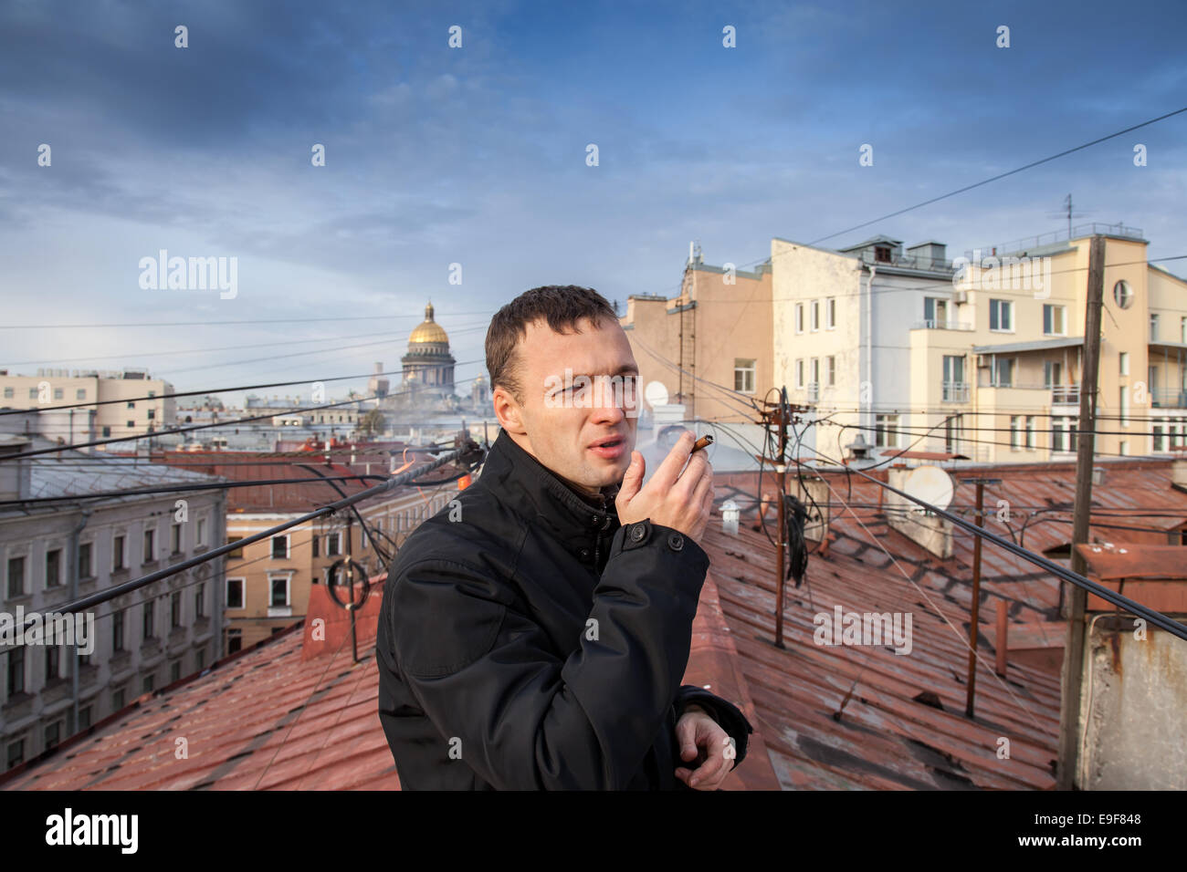 Young Caucasian man smokes cigar on the roof in central part of Saint ...