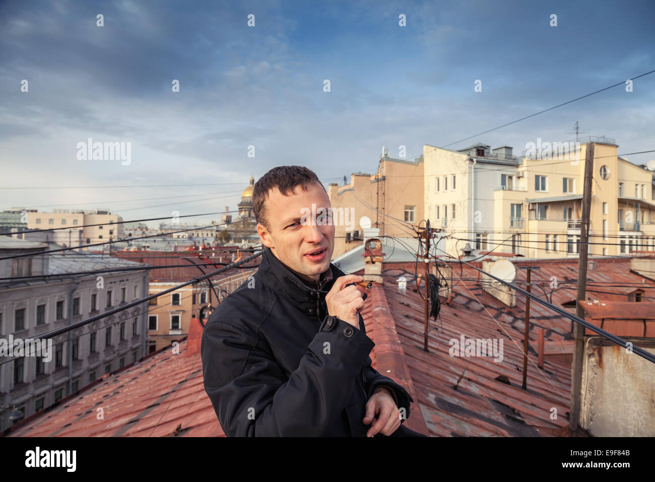 Young Caucasian man smokes cigar on the roof in central part of St ...