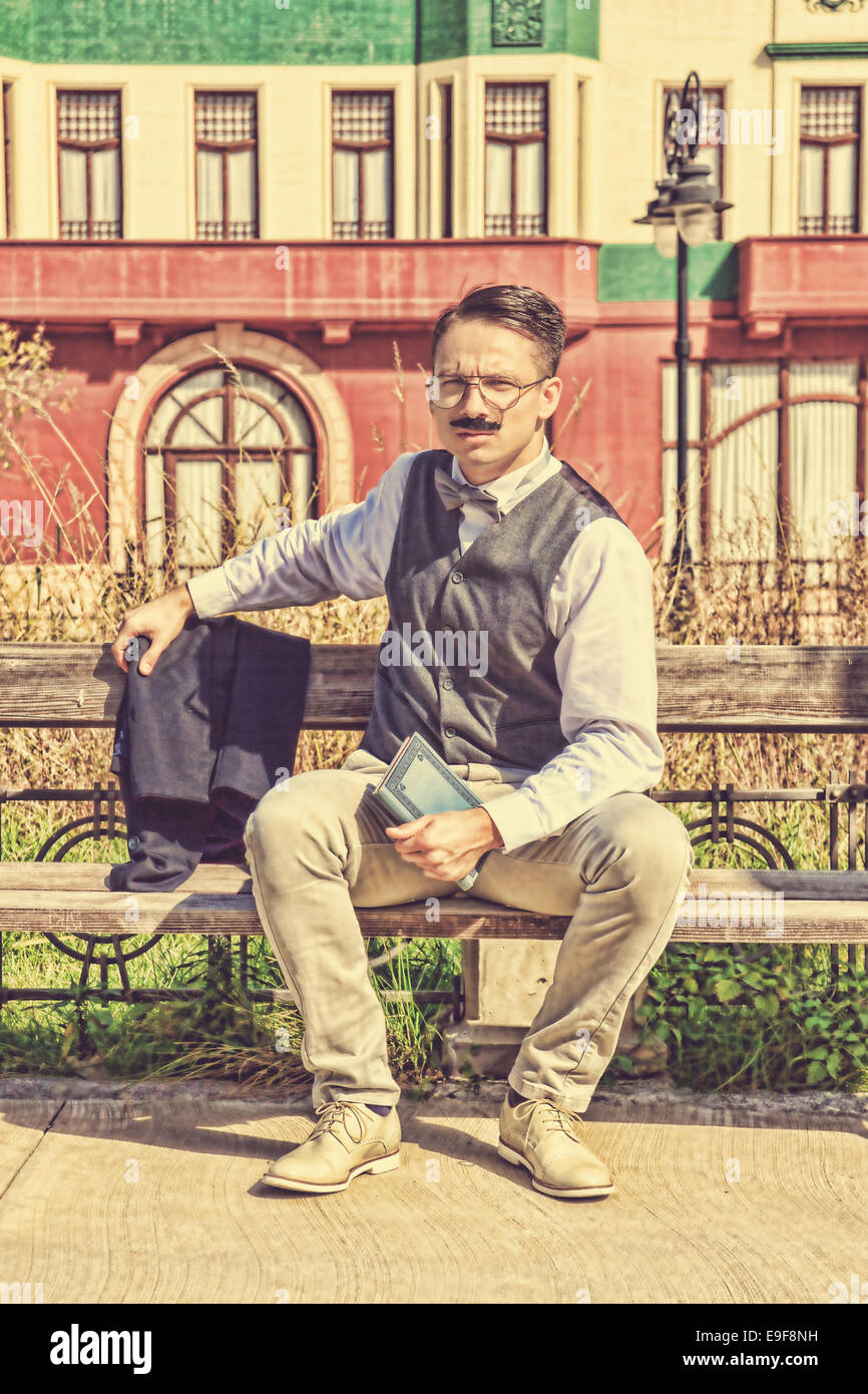 Elegant man sitting on the bench relaxing with a book outdoors on sunny ...