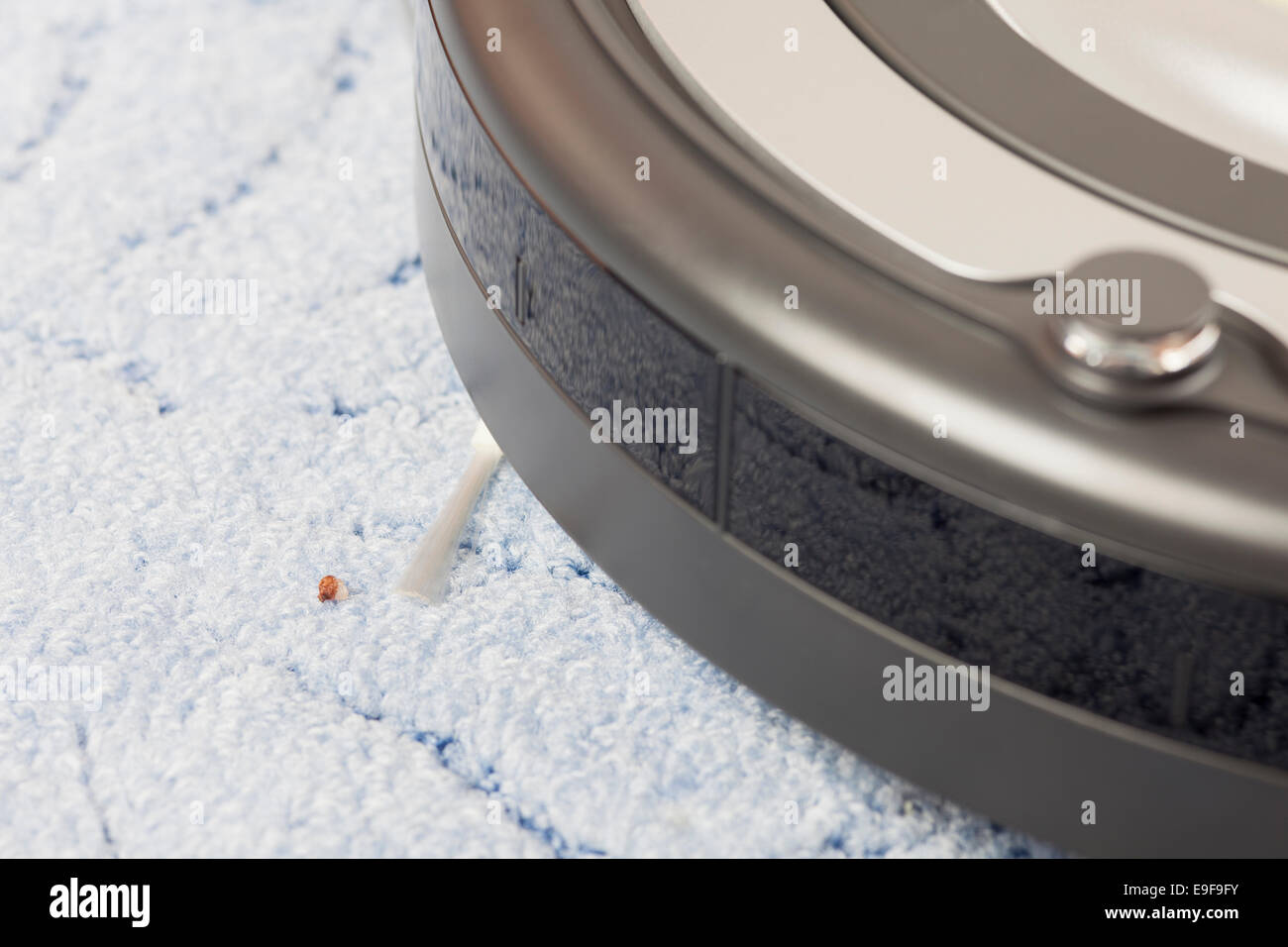 Vacuum Cleaning Robot on blue carpet with crumb Stock Photo - Alamy