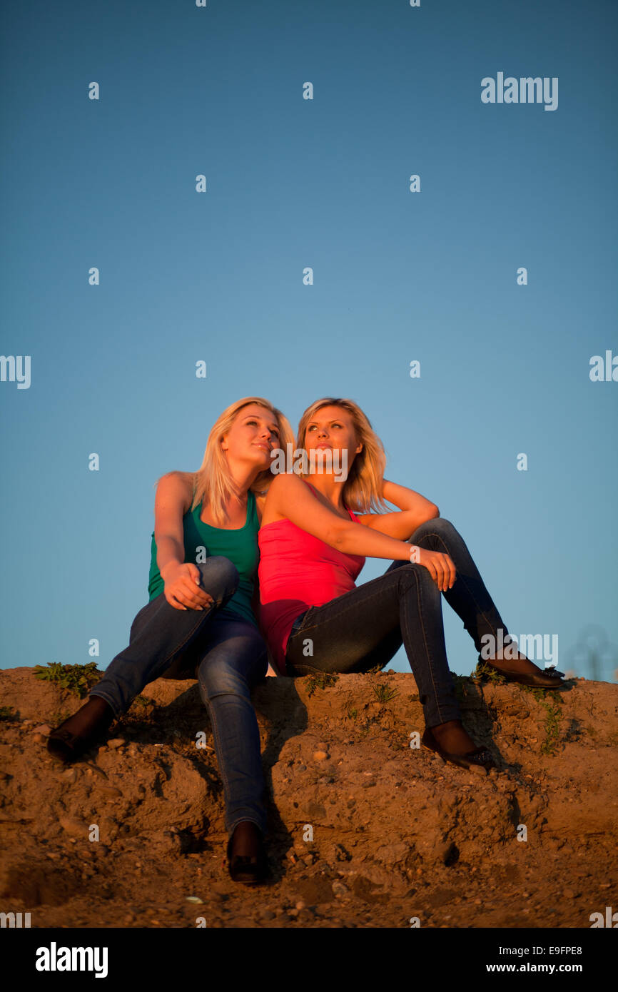 Two girls sit hugging and laughing at the blue sky Stock Photo - Alamy
