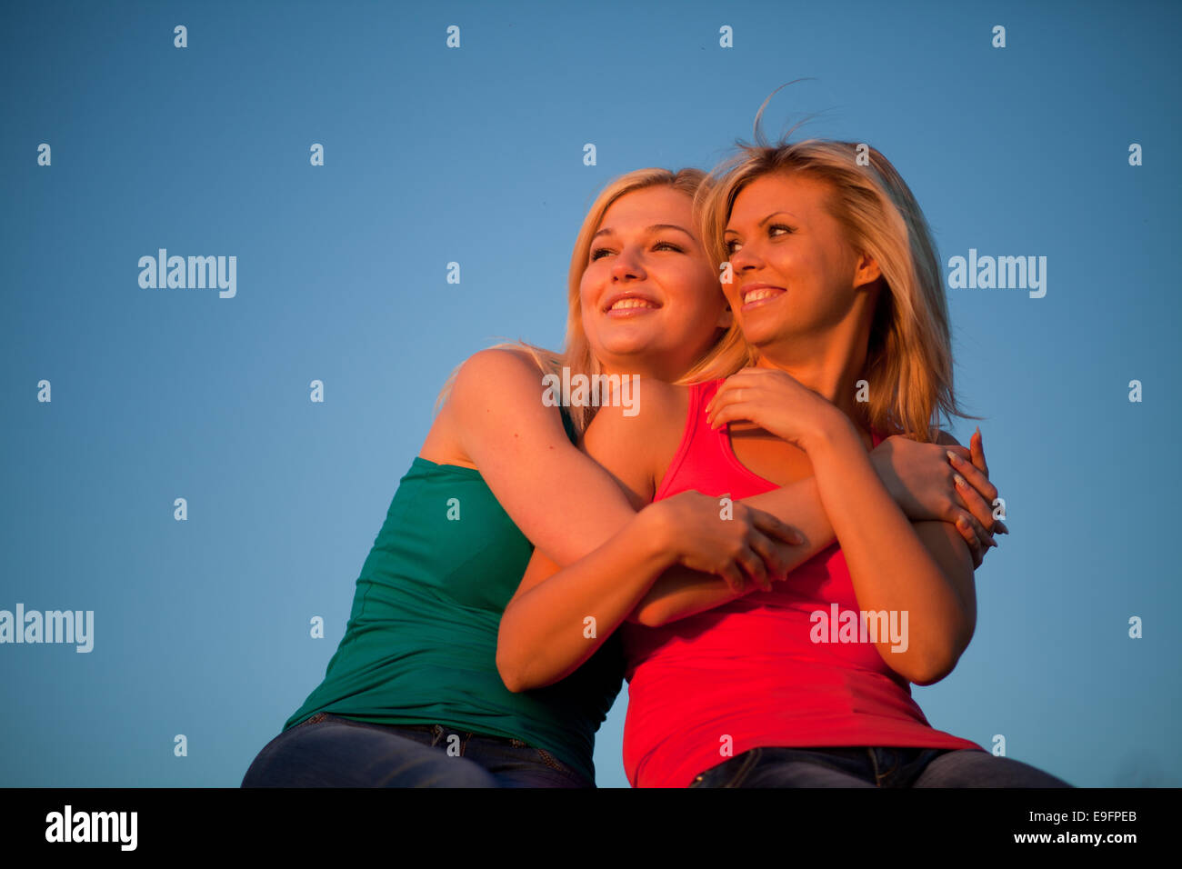 Two girls sit hugging and laughing at the blue sky Stock Photo - Alamy