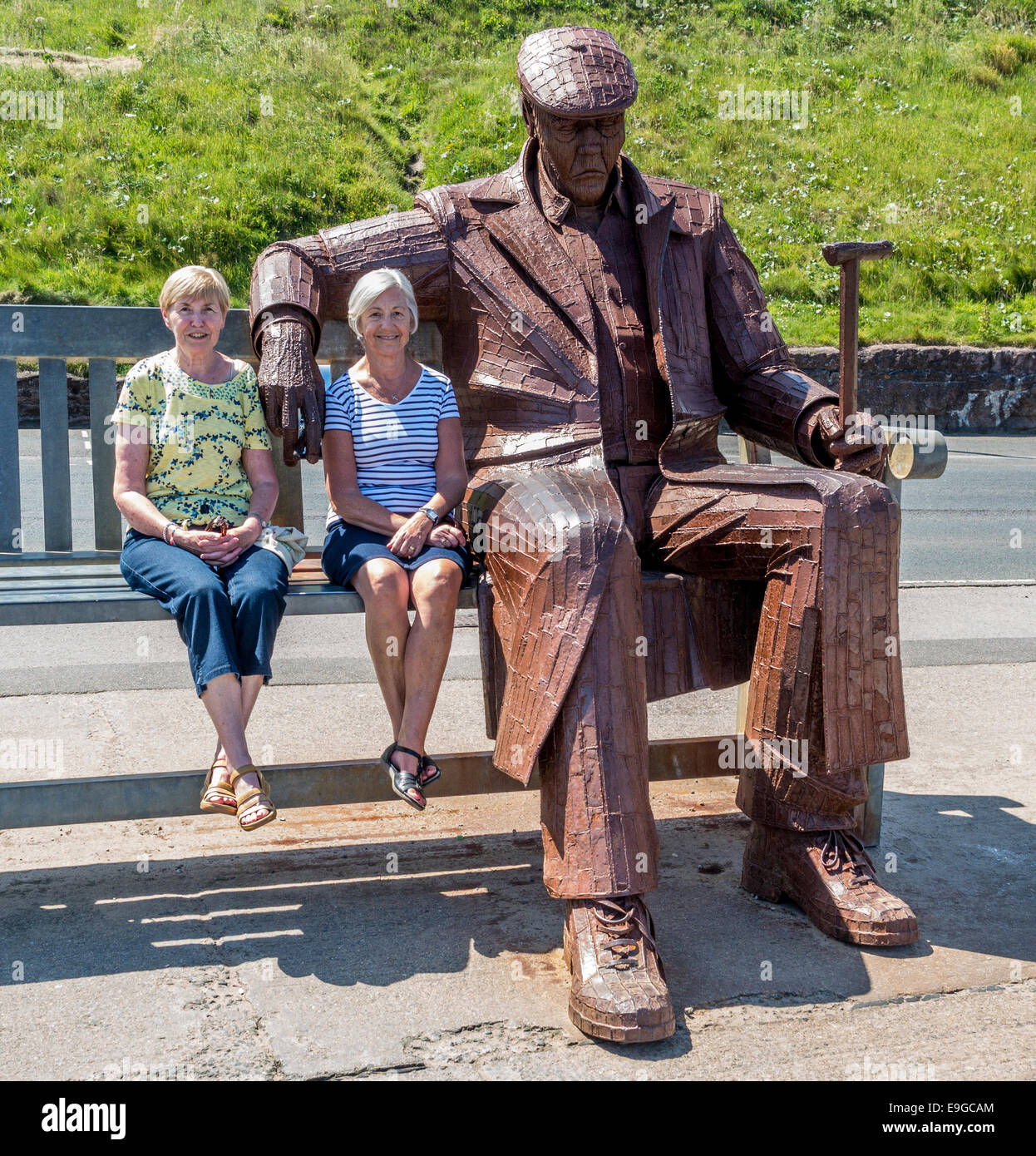 A giant metal man sat on a bench with two ladies alongside him Stock ...