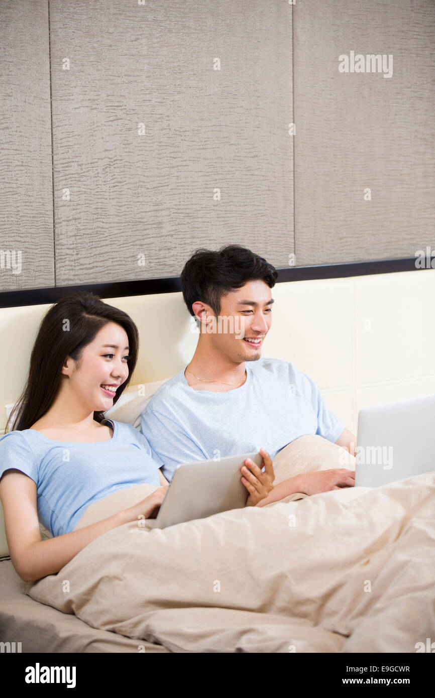 Young couple using wireless devices on bed Stock Photo - Alamy