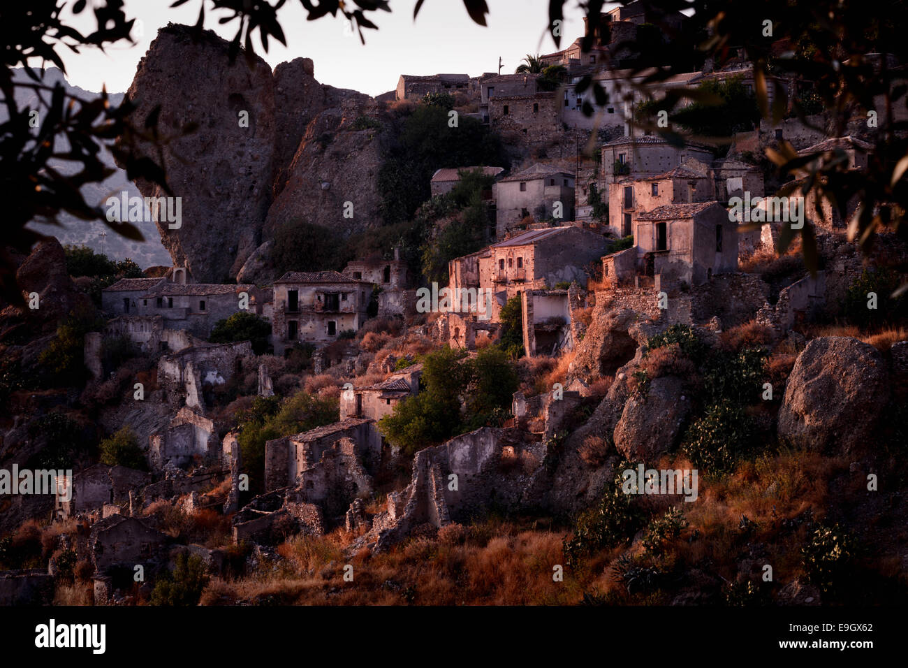 The abandoned village of Pentedattilo at sunset framed by blurred olive ...