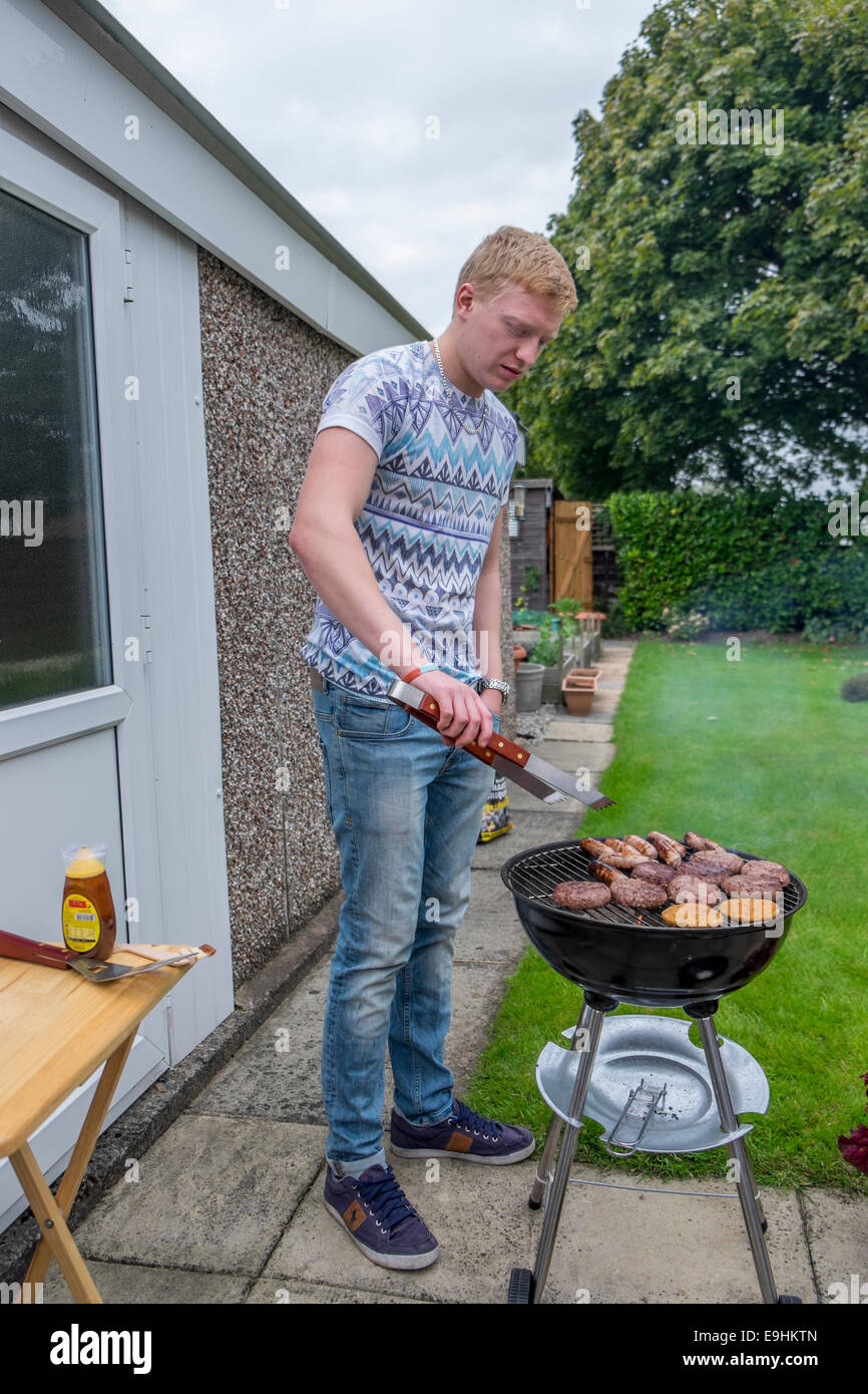 Young adult male trying to light a BBQ and cooking food in the summer ...